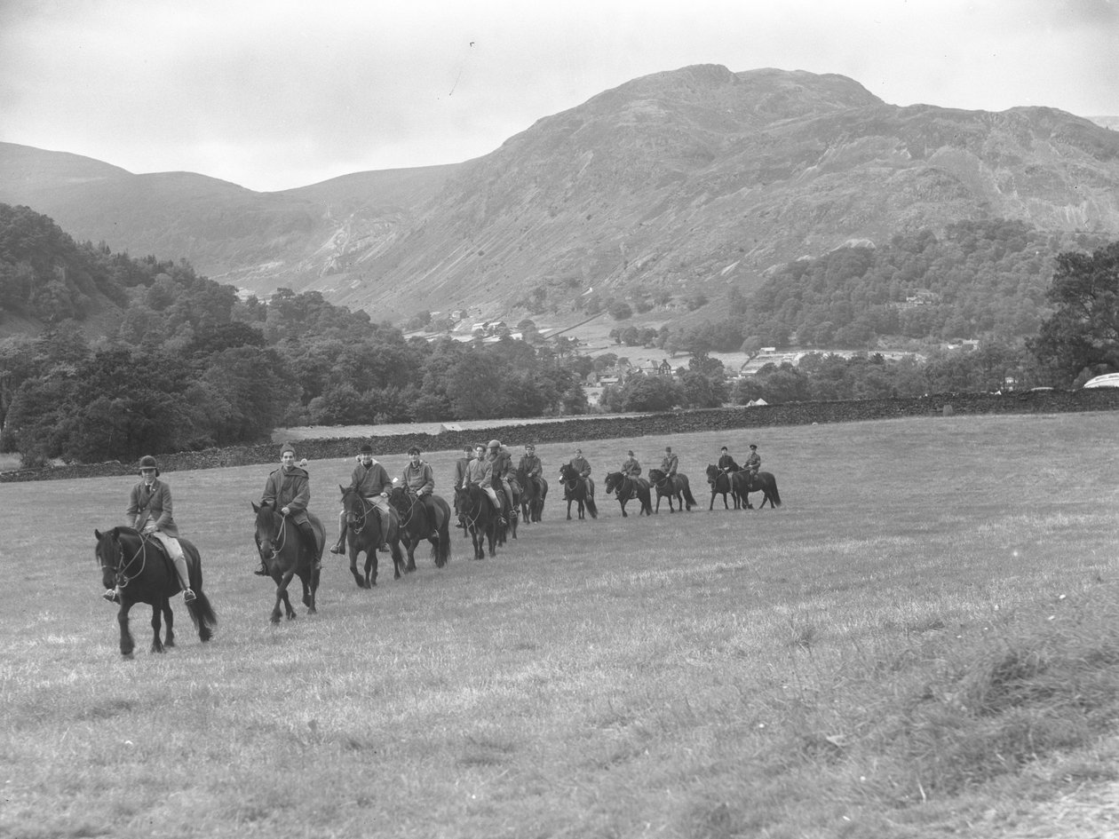 A group of men trekking in a line on ponies, fells in the background